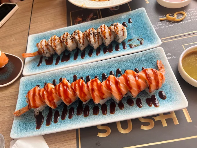 Due taglieri di uramaki al salmone e gambero con salsa teriyaki, serviti su piatti azzurri